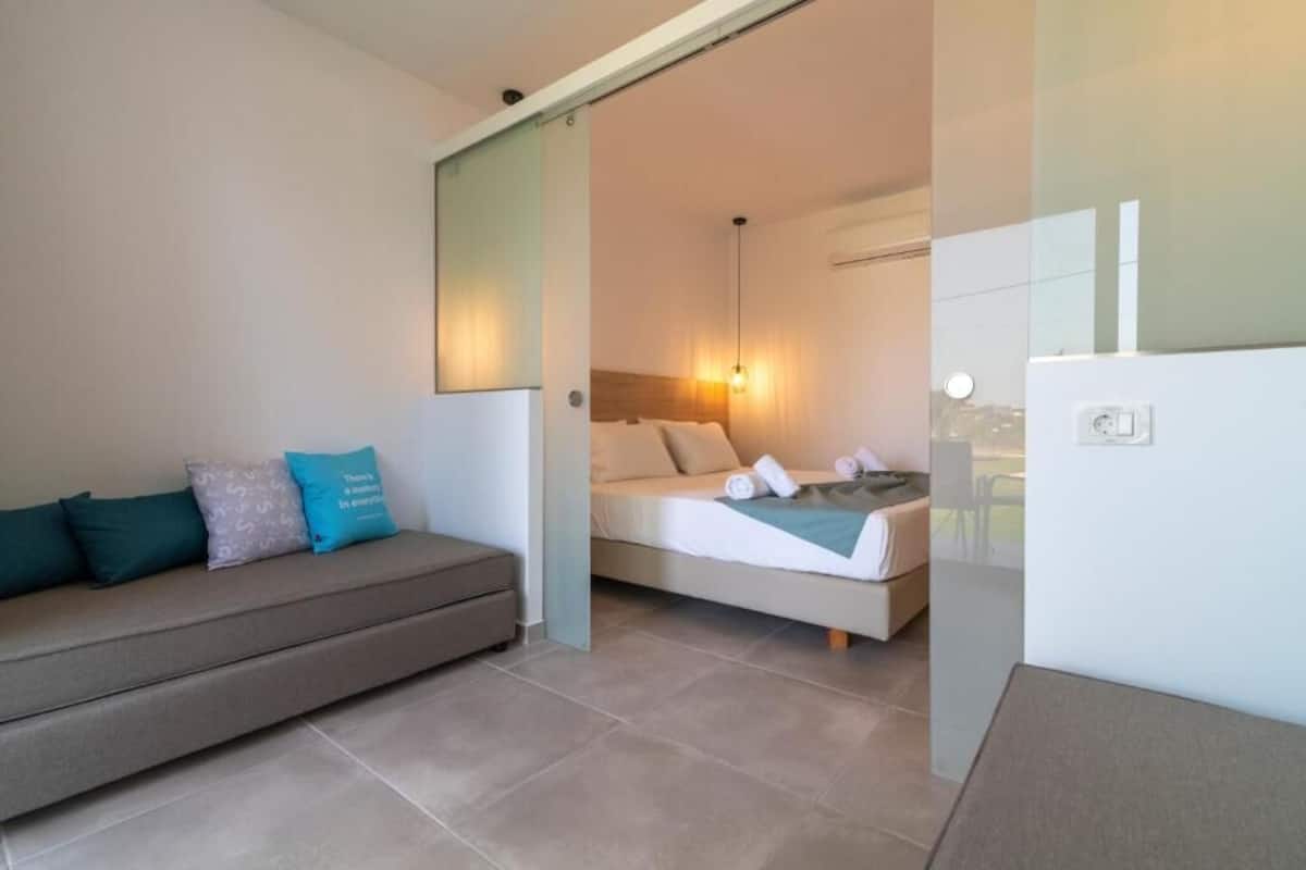 Quarto de hotel moderno com sofá, cama e divisória de vidro.
