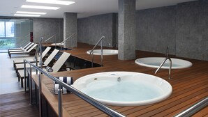 Uma área de spa moderna com duas banheiras de hidromassagem, piso de madeira e uma parede de vidro que oferece vista para o exterior.