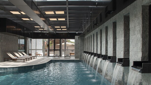 Piscina interior com cascata, espreguiçadeiras e parede de pedra.
