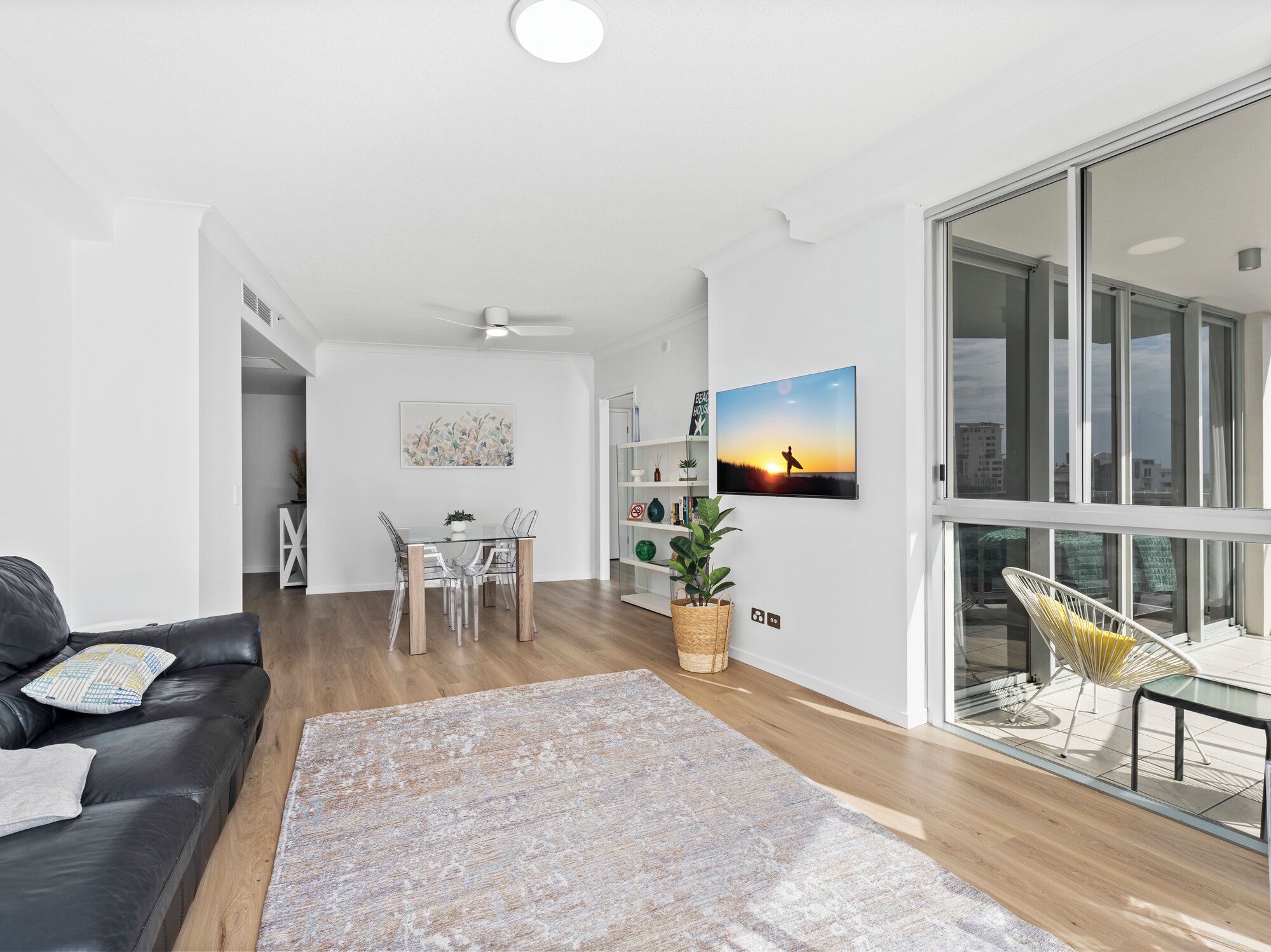 Uma sala de estar moderna com um sofá de couro preto, uma mesa de jantar de vidro e uma grande janela com vista para a paisagem urbana.