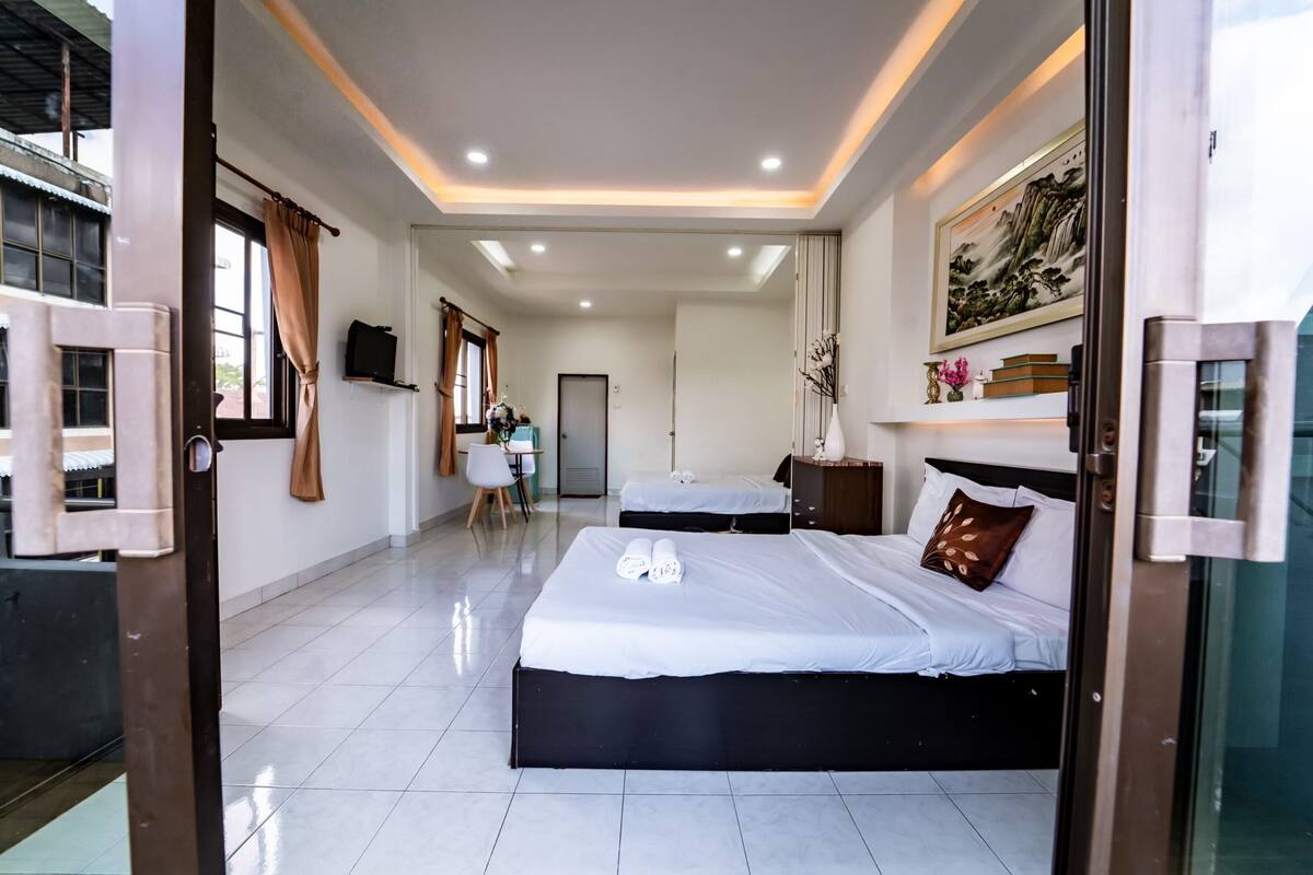 Quarto de hotel com duas camas, uma escrivaninha e uma janela grande com cortinas.