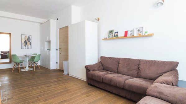 Uma sala de estar moderna com um sofá marrom, uma mesa de jantar com cadeiras e piso de madeira.