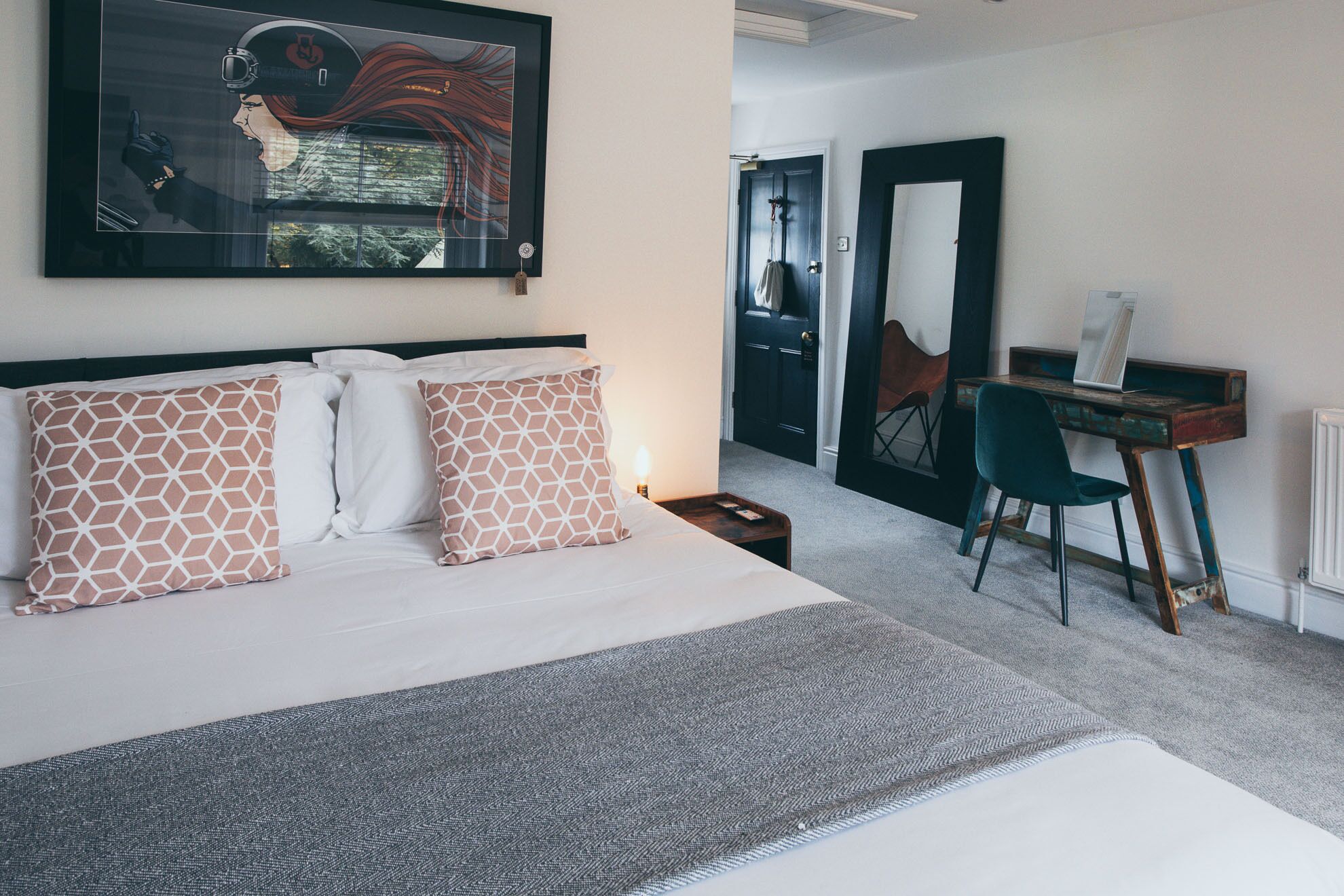 Quarto de hotel moderno com uma cama grande, uma secretária com um computador portátil e uma obra de arte emoldurada na parede.