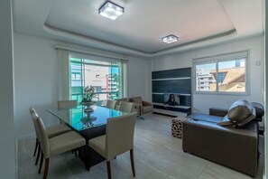 Uma sala de estar moderna com uma mesa de jantar de vidro, cadeiras bege, um sofá e uma TV.