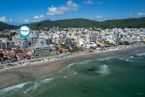 Paisagem costeira com praia, edifícios e montanhas ao fundo.