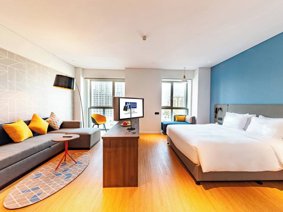 Quarto de hotel moderno com cama, sofá, escrivaninha e vista para a cidade.