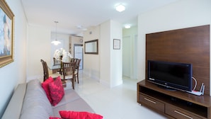 Sala de estar com sofá, televisão e área de jantar.