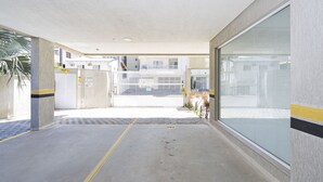 Uma área de estacionamento coberta com entrada por portão, piso de concreto e uma grande janela à direita.