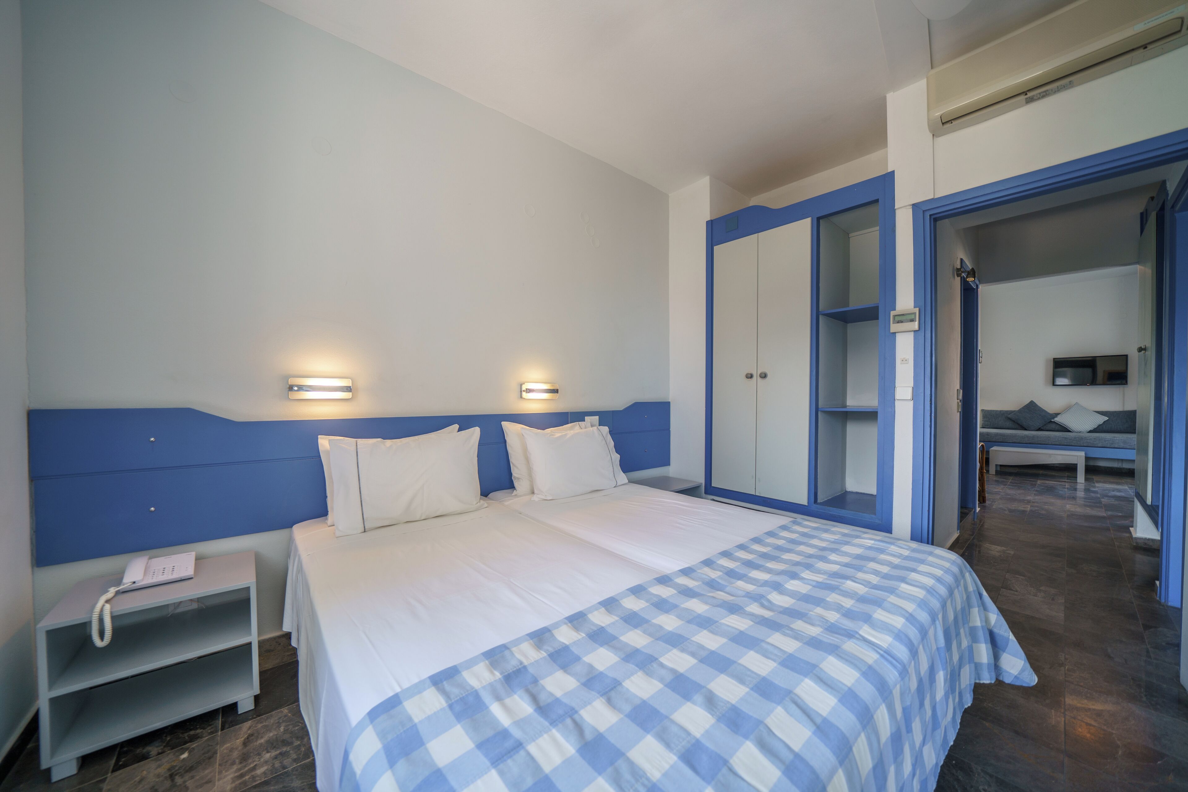 Quarto de hotel com cama, abajures, mesa de cabeceira, guarda-roupa e um espaço de estar com um banco.