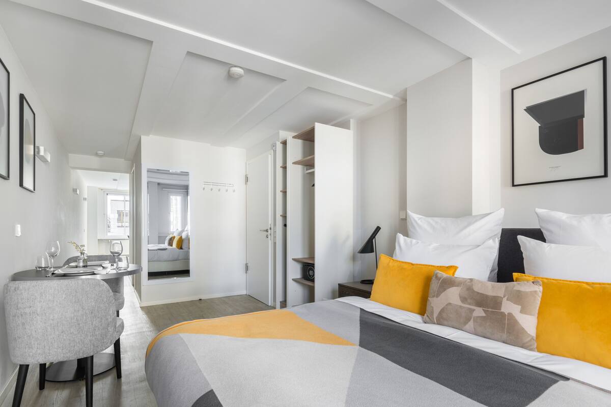 Quarto de hotel moderno com uma cama, uma mesa e uma cadeira. Um banheiro é visível por uma porta aberta.