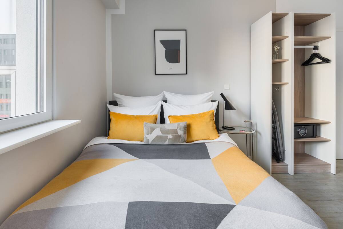 Quarto moderno com cama, mesa de cabeceira, cabideiro e armário embutido.