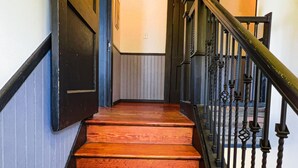 Uma escada de madeira com corrimão preto, que leva a um patamar com luminária.