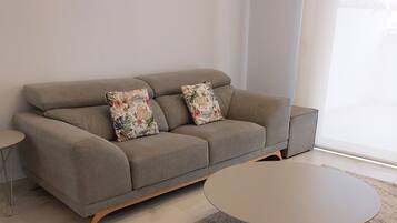 Uma sala de estar moderna com um sofá cinza, duas almofadas florais, uma mesa de centro redonda e um tapete estampado.