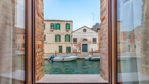 Um canal estreito com barcos, edifícios com janelas em arco e um céu limpo.