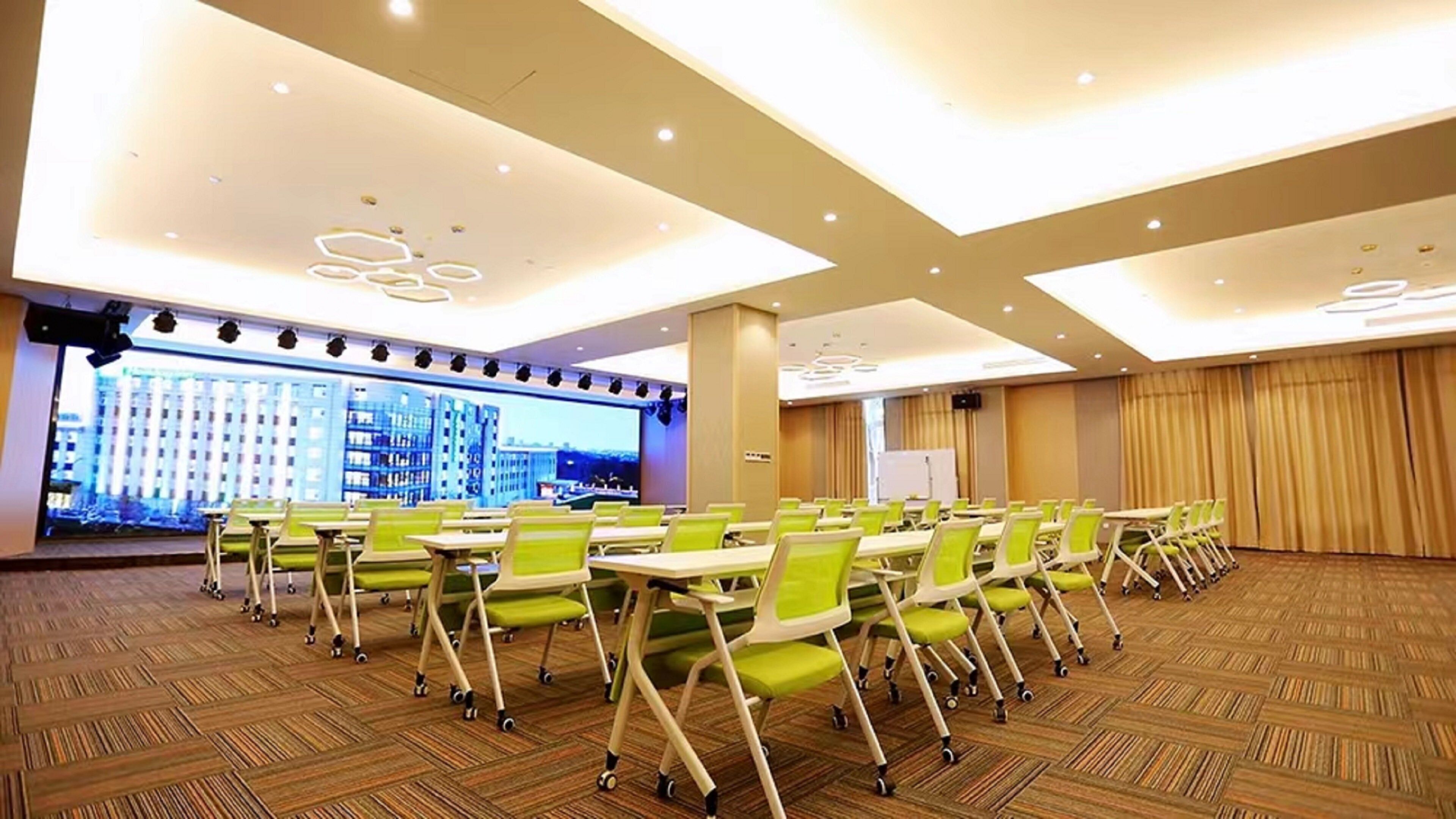 Sala de conferência com cadeiras verdes, uma tela grande e vista para a cidade.