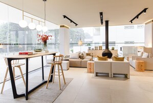 Uma sala de estar moderna com área de jantar, janelas amplas e cozinha ao fundo.
