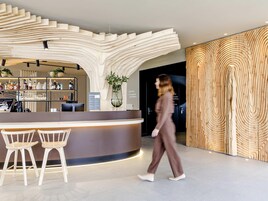Uma área de recepção moderna com balcão curvo, banquetas e painel de madeira com design exclusivo.