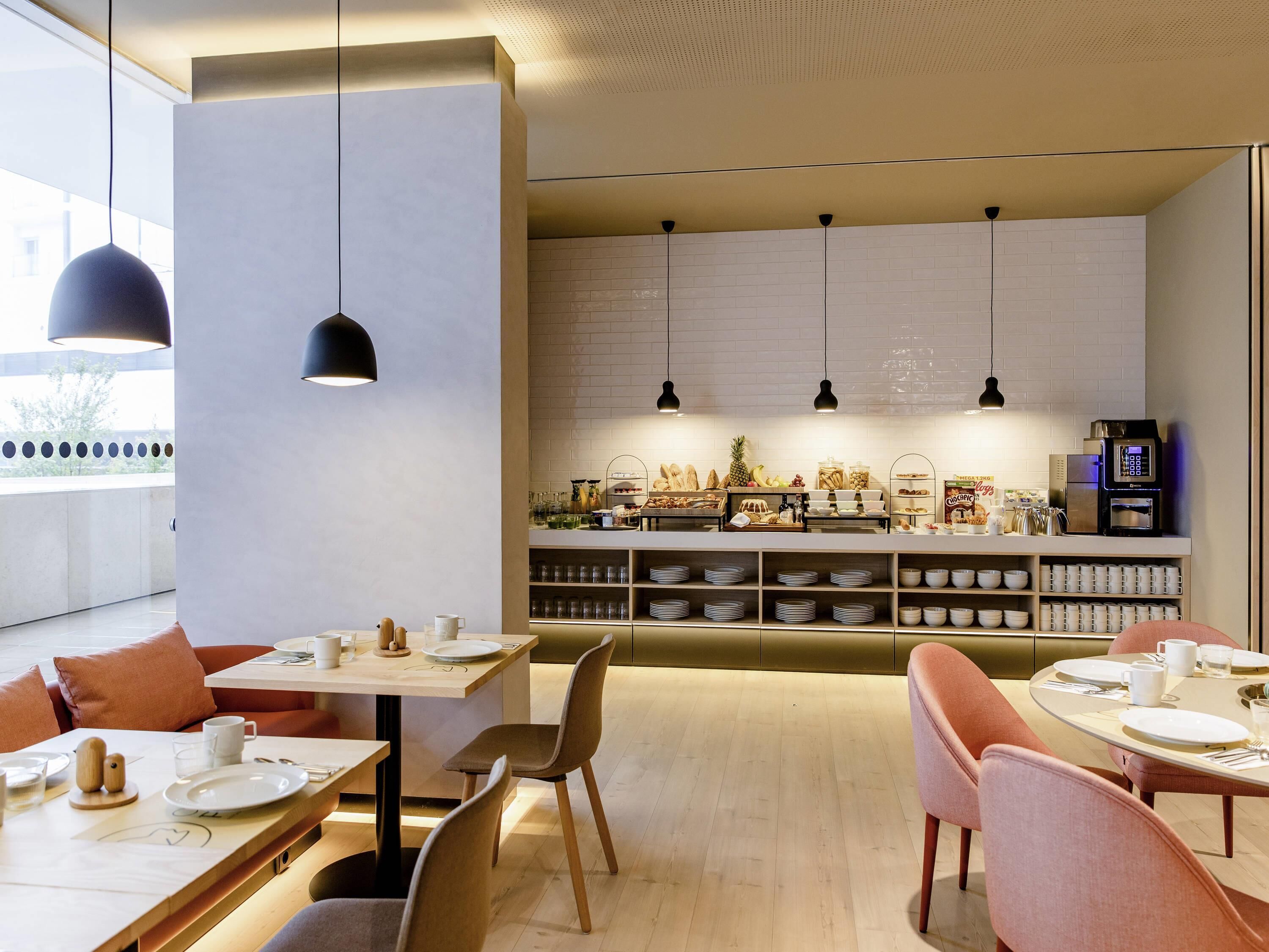 Uma área de jantar moderna com mesas, cadeiras e um balcão de buffet com comida e bebidas.