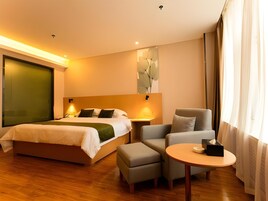 Quarto de hotel com uma cama, uma cadeira, uma mesa pequena e uma mesinha de cabeceira.