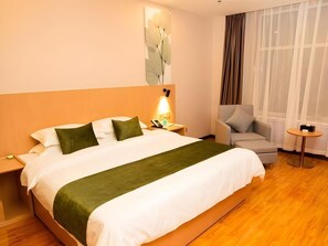 Quarto de hotel com uma cama grande, mesa de cabeceira com abajur, uma cadeira e uma mesinha.