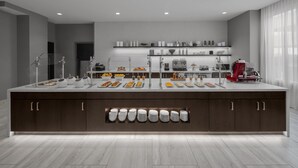Uma cozinha moderna com ilha central, eletrodomésticos embutidos e diversos alimentos expostos na bancada.