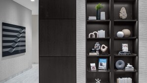 Um interior moderno com um armário de madeira escura, parede texturizada e uma estante com diversos objetos decorativos e livros.