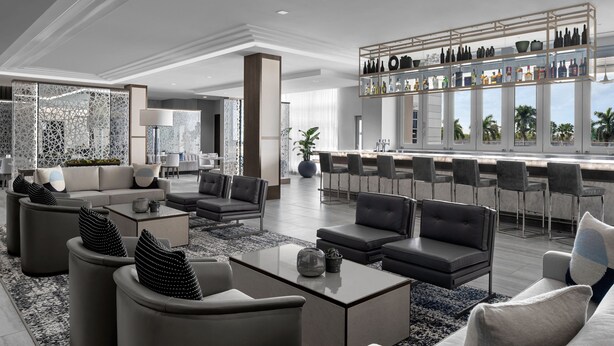 Uma área de estar moderna com sofás, uma mesa de centro e um bar com prateleiras cheias de garrafas.