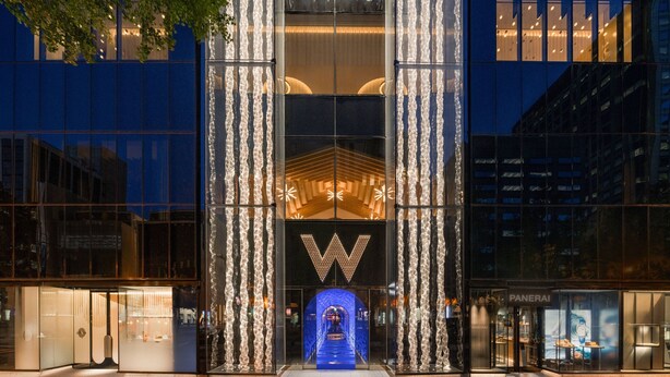 Um edifício moderno com um logotipo 'W' em destaque, fachada de vidro e entrada iluminada em azul.