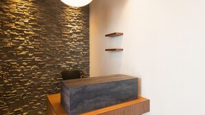 Uma receção com parede de pedra, balcão de madeira e duas prateleiras fixadas na parede.