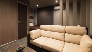 Quarto de hotel moderno com sofá bege, porta de madeira e parede de cor escura.