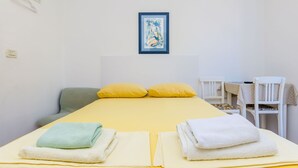 Cama bem arrumada com roupa de cama amarela e duas almofadas, uma pequena mesa de escritório com cadeira, e uma obra de arte emoldurada acima da cama.