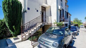 Um carro prateado estacionado em frente a um edifício com uma escadaria que leva a uma varanda.