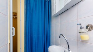 Um banheiro com pia branca, cortina de chuveiro azul e um dosador de sabão na parede.