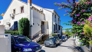Uma rua estreita com carros estacionados e um edifício branco com varanda.