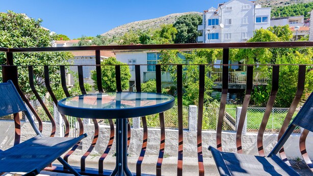 Varanda com mesa de vidro e duas cadeiras, com vista para uma colina com edifícios.