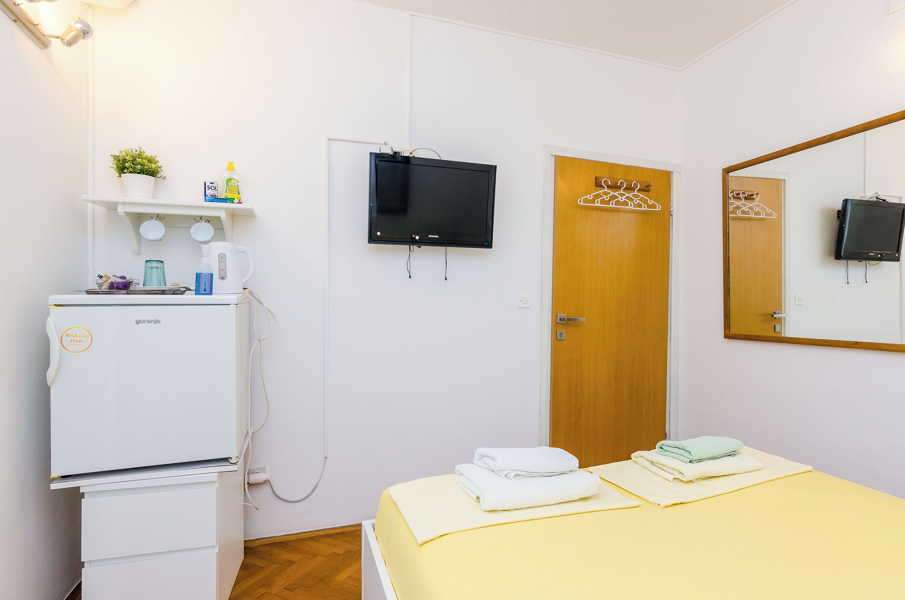 Quarto de hotel com cama, televisão na parede, porta de madeira e frigorífico.
