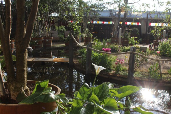 Um jardim com lago, plantas em vasos e uma ponte de madeira.