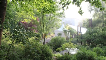 Um jardim exuberante com um gazebo, um caminho e um edifício ao fundo.