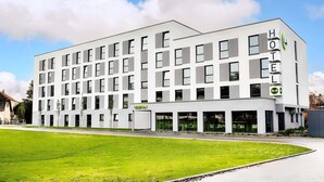 Um hotel moderno com fachada branca, várias janelas e um gramado verde à frente.