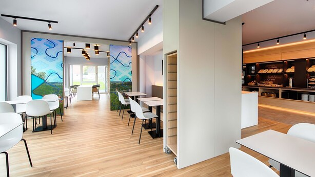 Um espaço de escritório moderno com mobiliário branco, um mural com designs abstratos e uma área de café com um painel de exibição do menu.