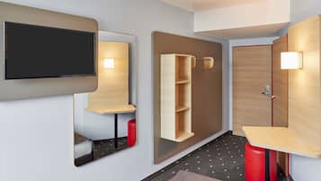 Quarto de hotel moderno com televisão de tela plana, prateleiras embutidas, um banquinho vermelho e uma porta de madeira.