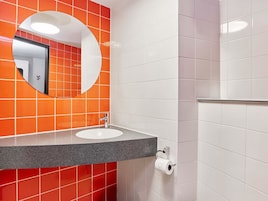 Casa de banho com lavatório, espelho e dispensador de papel higiénico.