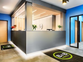 Uma área de recepção com design moderno, destacando um balcão de atendimento, uma planta e um logotipo na parede.