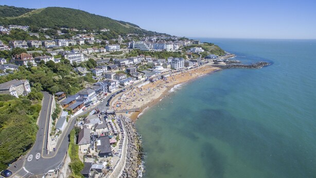 Vista aérea de uma cidade costeira com praia, edifícios residenciais e um mar azul límpido.