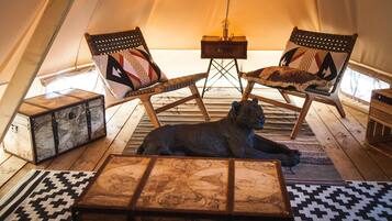 Interior de uma tenda com duas cadeiras de madeira, uma mesa pequena e um baú grande.