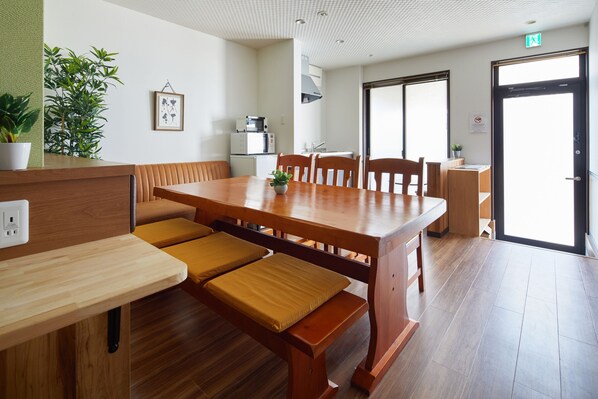 Uma sala de jantar com mesa e bancos de madeira, área de cozinha com micro-ondas e fogão, e uma porta com placa de saída.