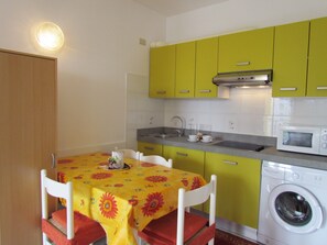 Uma cozinha compacta com uma mesa posta para dois, uma máquina de lavar e um micro-ondas.