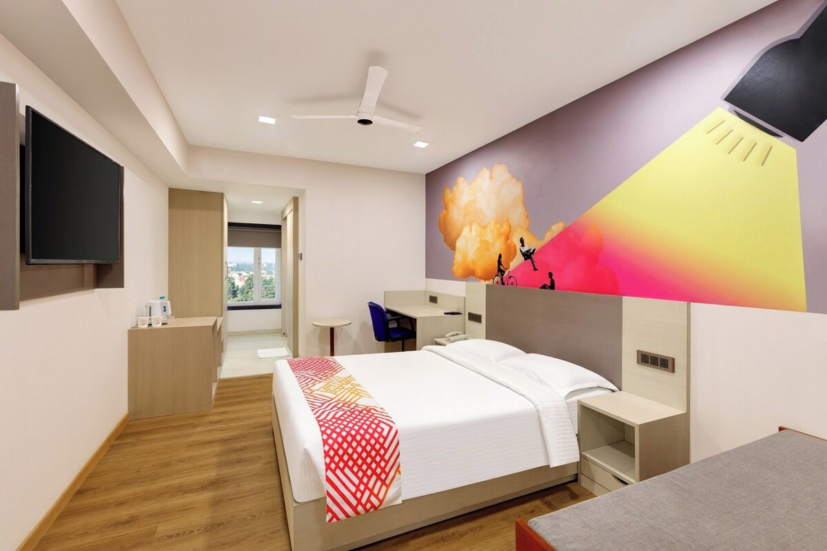 Quarto de hotel moderno com cama, mesas de cabeceira, escrivaninha, cadeira, TV de tela plana e uma grande janela.