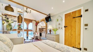 Quarto com cama, televisão, porta de madeira e janela com cortinas.
