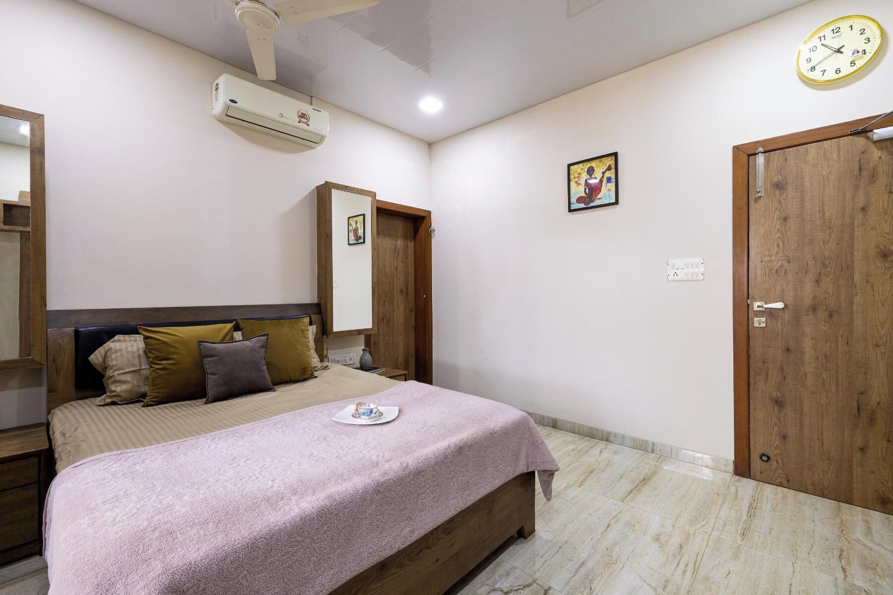 Quarto com cama, guarda-roupa de madeira, um pequeno relógio de parede e ar condicionado.